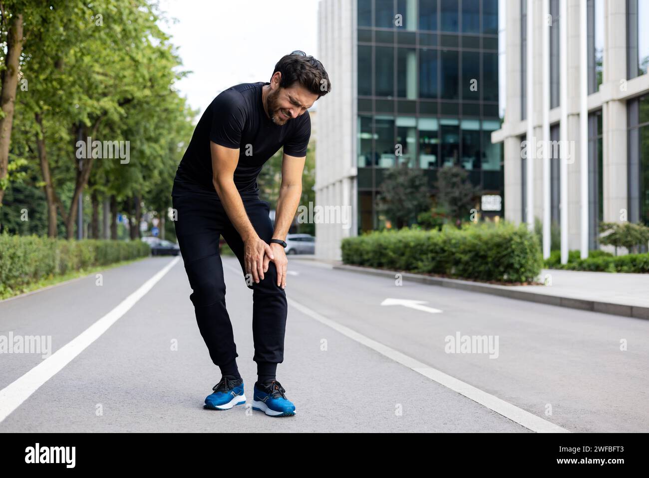 A young male runner and sportsman stands on the street of the city in ...