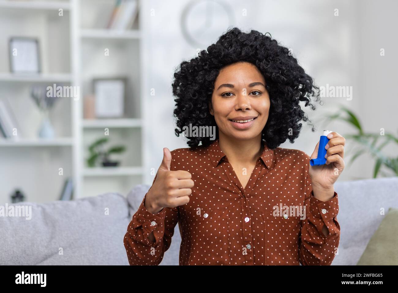Cheerful young woman with curly hair giving a thumbs up in a cozy ...