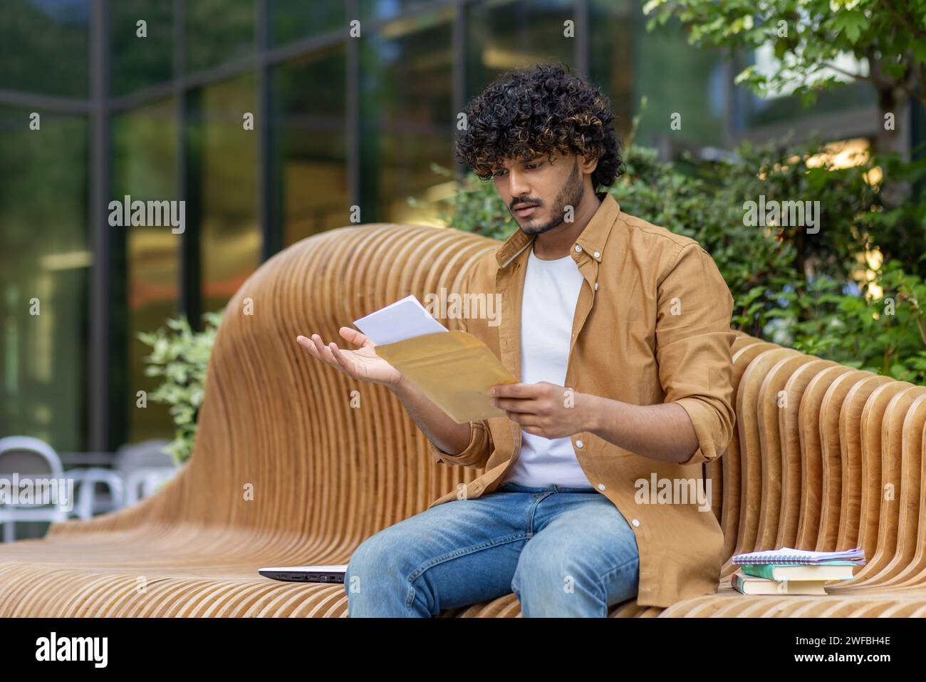 Shocked young Indian male student sitting on bench near office center ...