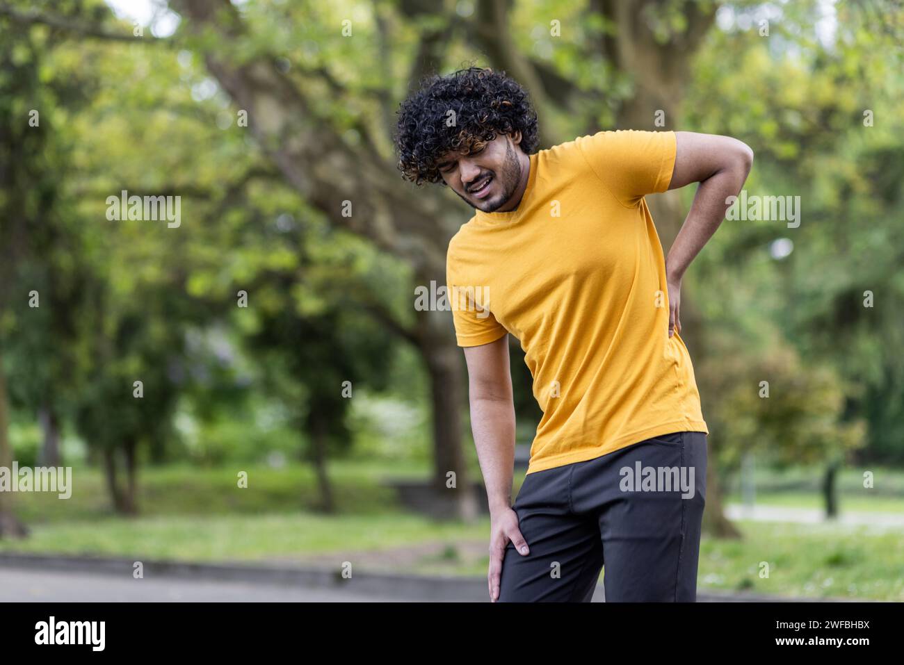 A young Indian male athlete is standing in the park, bent over and ...