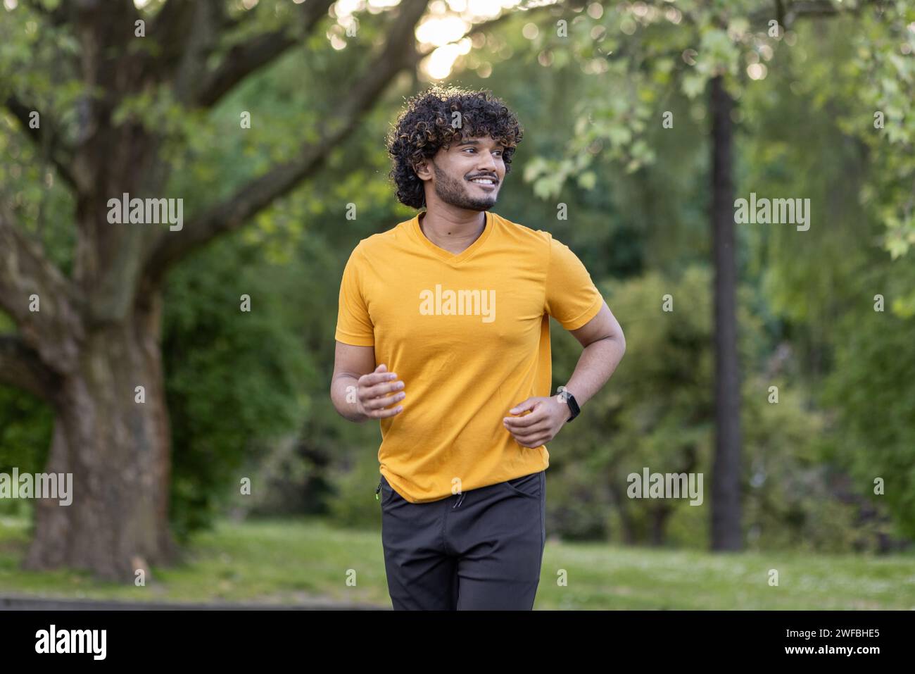 Smiling young Indian man running in the park, doing a morning jog and ...