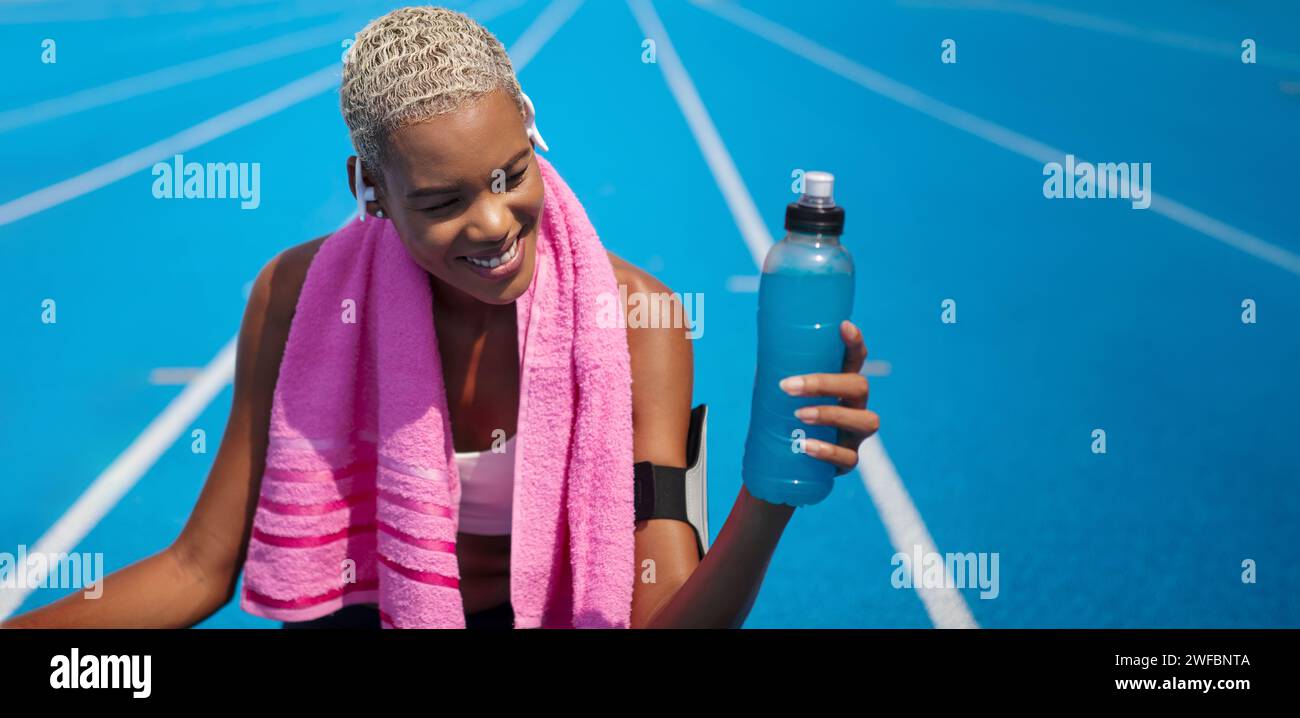 Smiling female athlete drinking energy drink from bottle after running ...