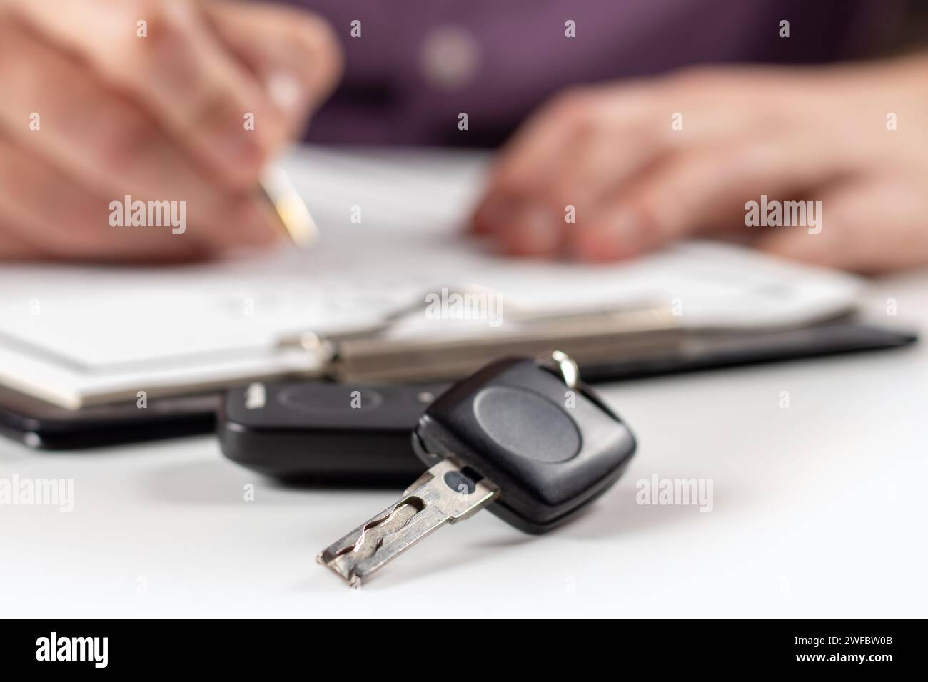 Car keys on desk with man signing purchase documents in background ...