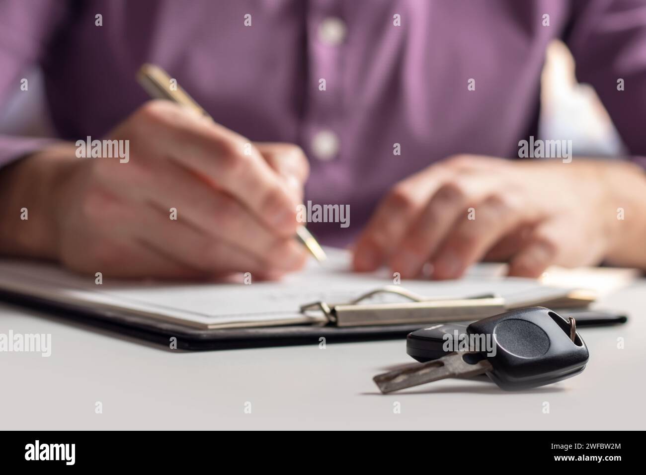 Car keys on desk with man signing purchase documents in background ...
