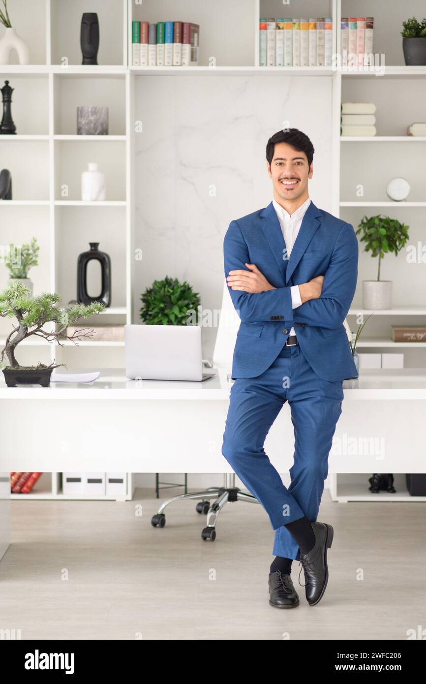 A confident Hispanic businessman stands with his arms crossed in a ...