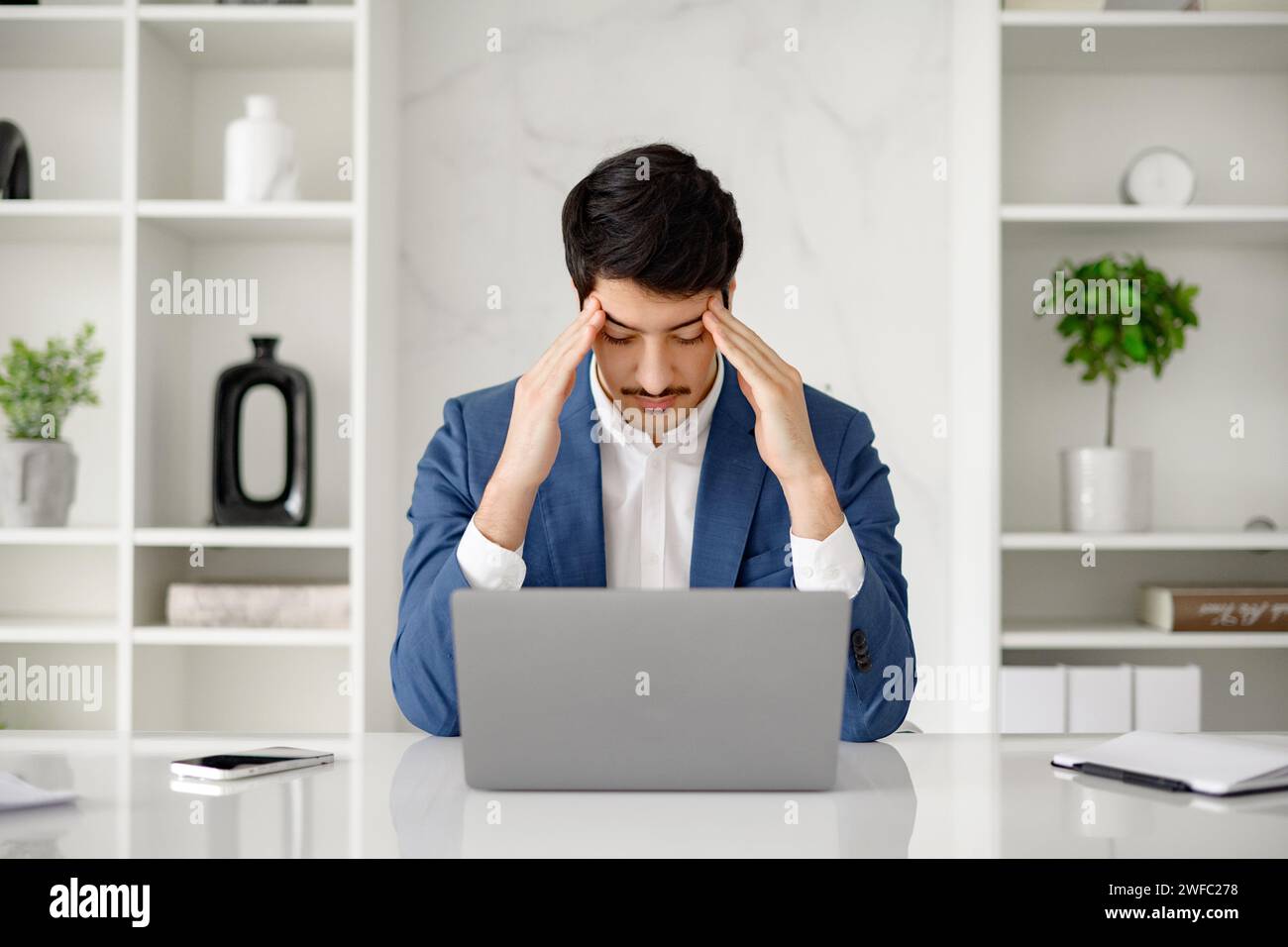 A Hispanic businessman experiences stress and headache while working on ...