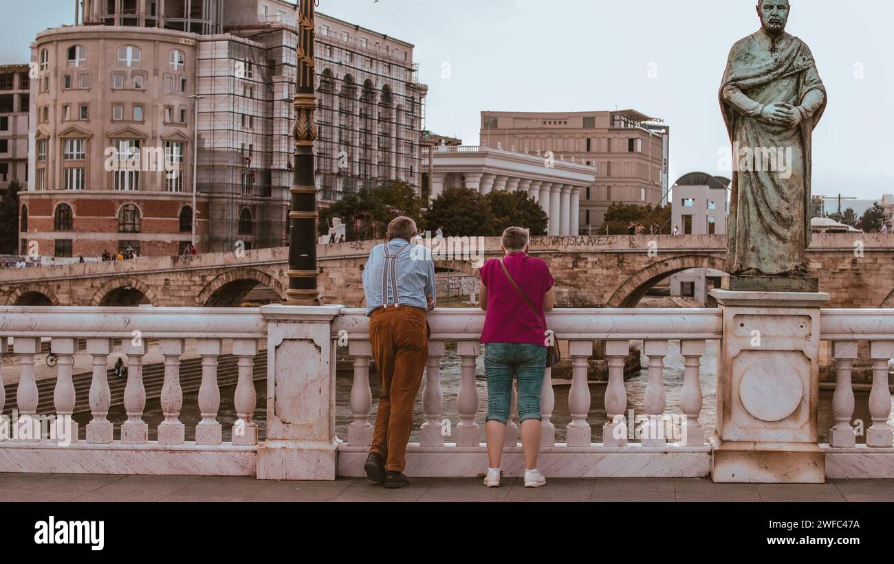 Two individuals standing on a bridge adjacent to a saintly statue of ...