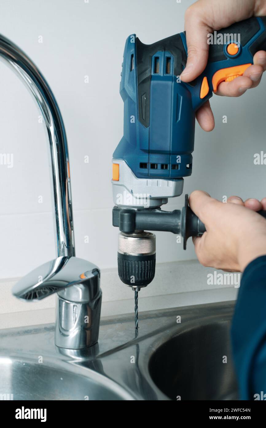 a caucasian man, wearing blue overalls, makes a hole in a metal kitchen ...