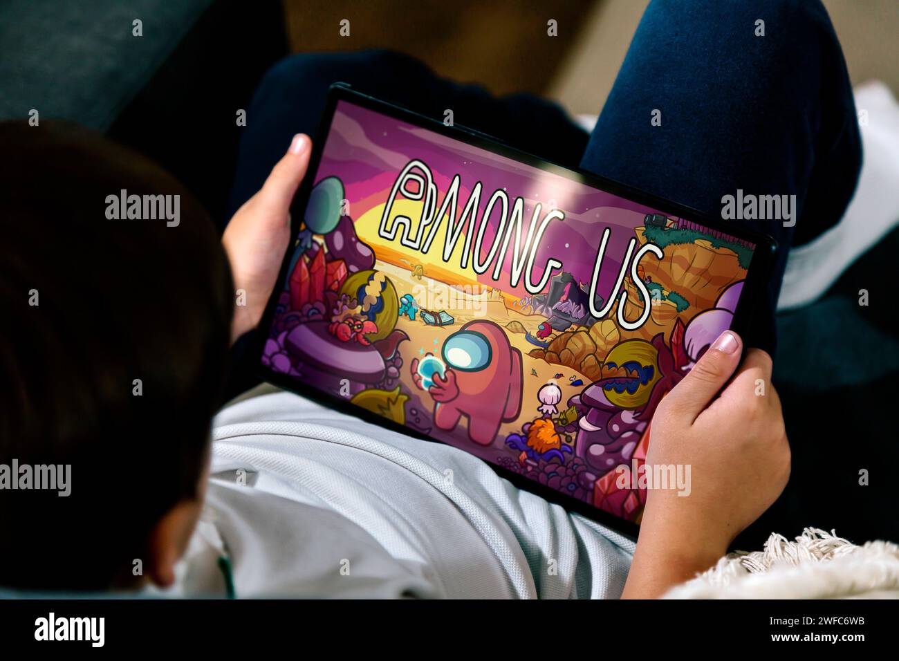 Little boy playing Among Us on a tablet, on the couch at home. It is a ...