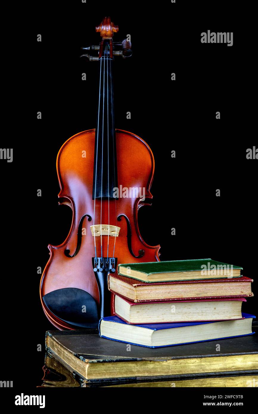 Old books with violin on a reflective black base and black background ...