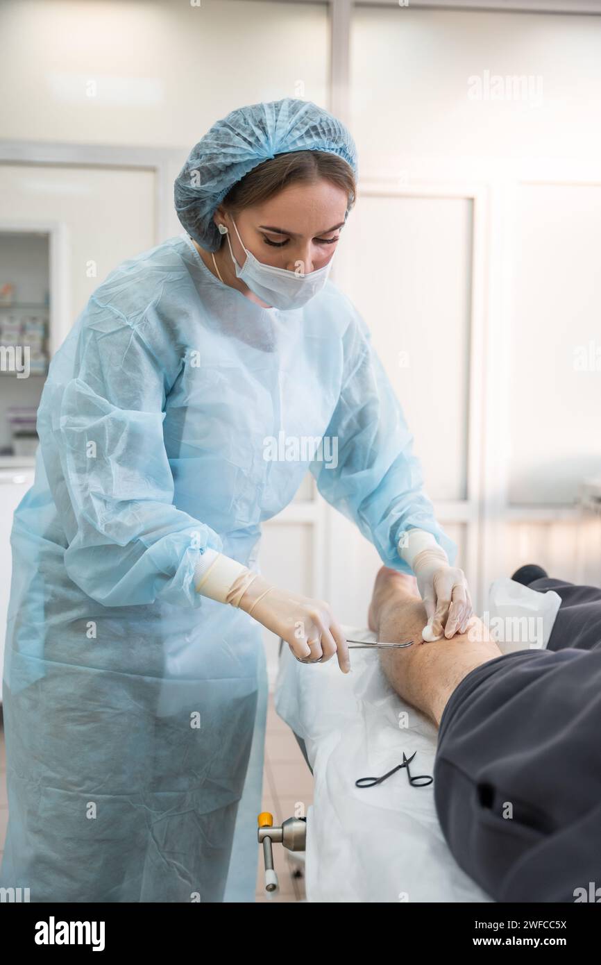 Young dermatologist surgeon stitching up a wound after skin surgery ...