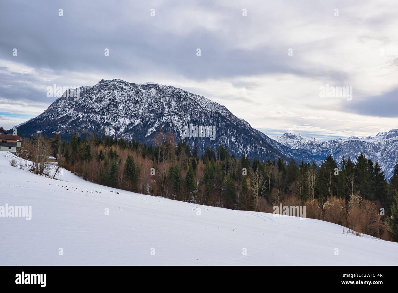 Snow-covered hill with towering mountains of the Hallstatt-Dachstein ...