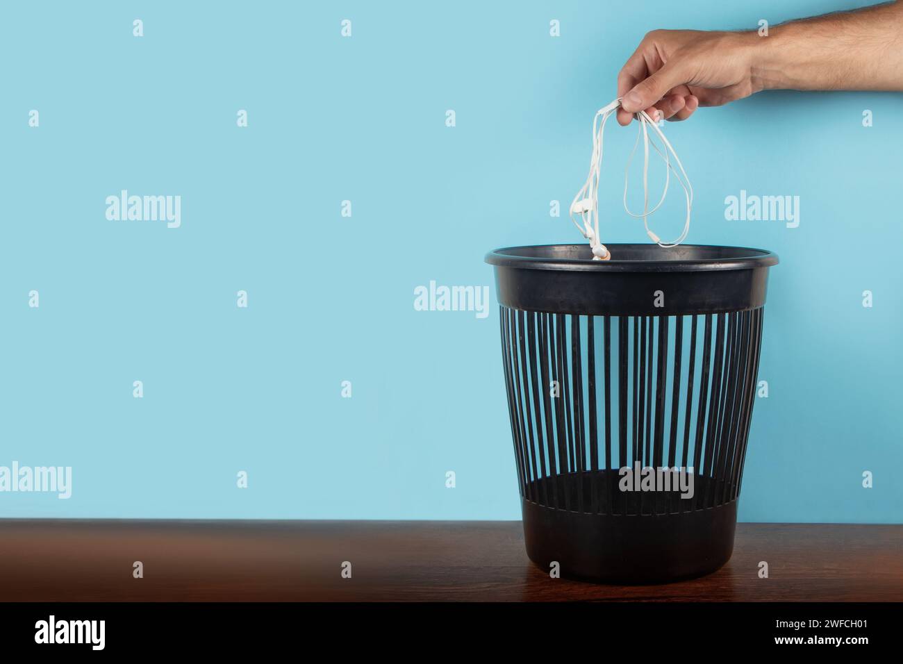 Hand throwing old shabby decrepit headphones away, trash bin ...