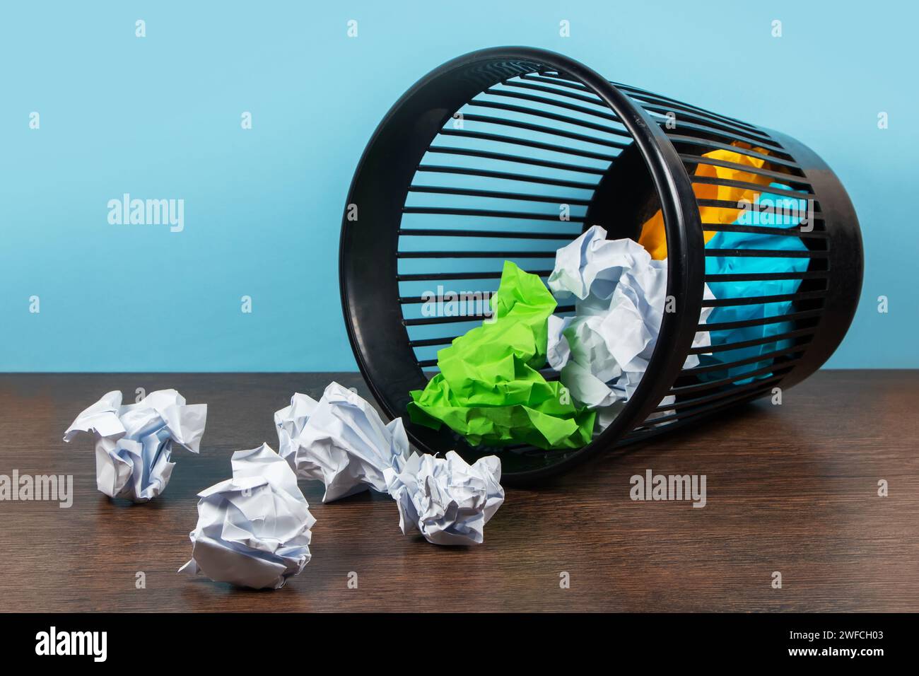 Overturned trash can with crumpled paper balls on a blue background ...