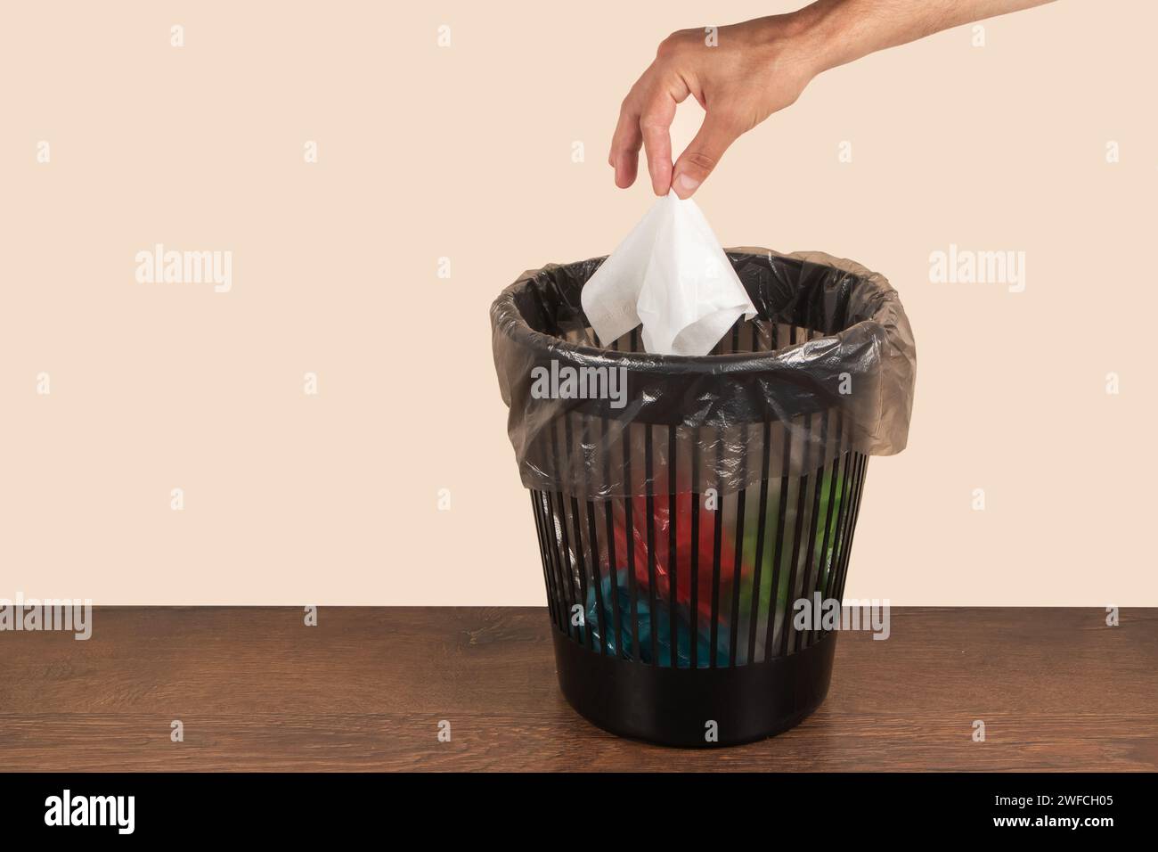 Man putting paper tissue into trash bin on light brown background Stock ...