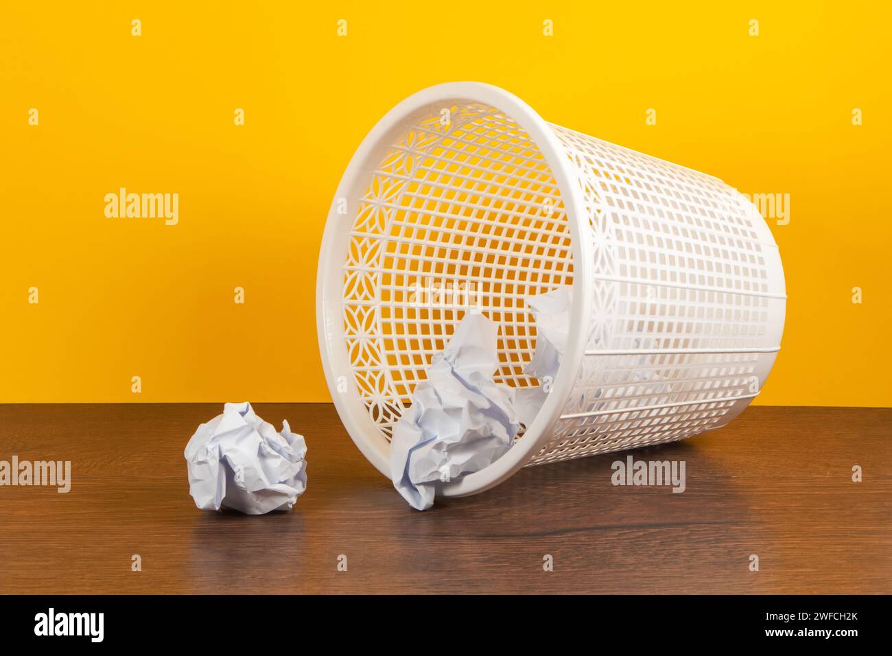 Overturned trash can with crumpled paper balls on a yellow background ...