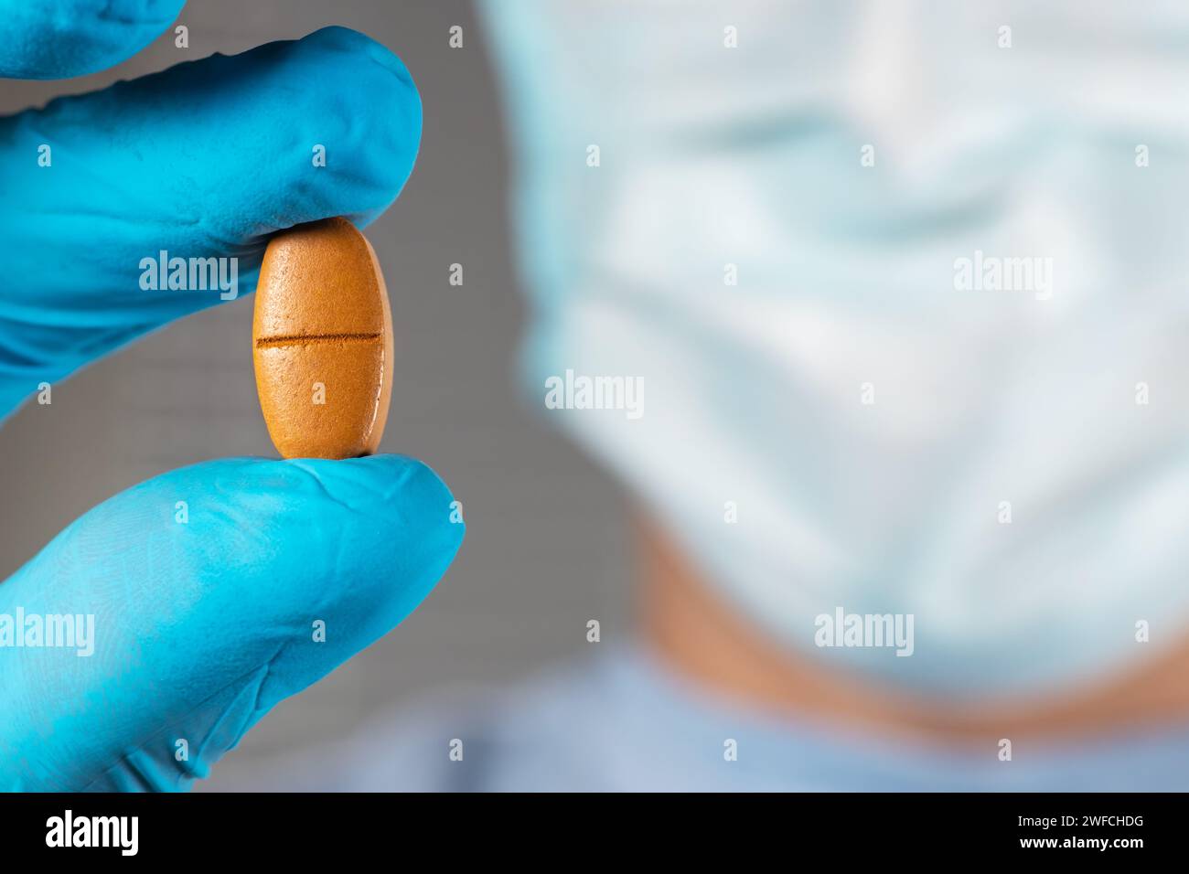 Doctor in mask holding a brown pill with fingers in gloves in the ...