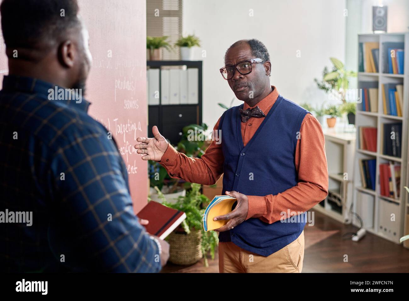 Portrait of Black college professor talking to student standing by ...