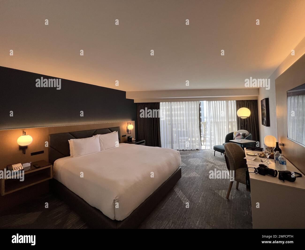 Modern hotel room interior with king-sized bed, desk area, and floor-to ...