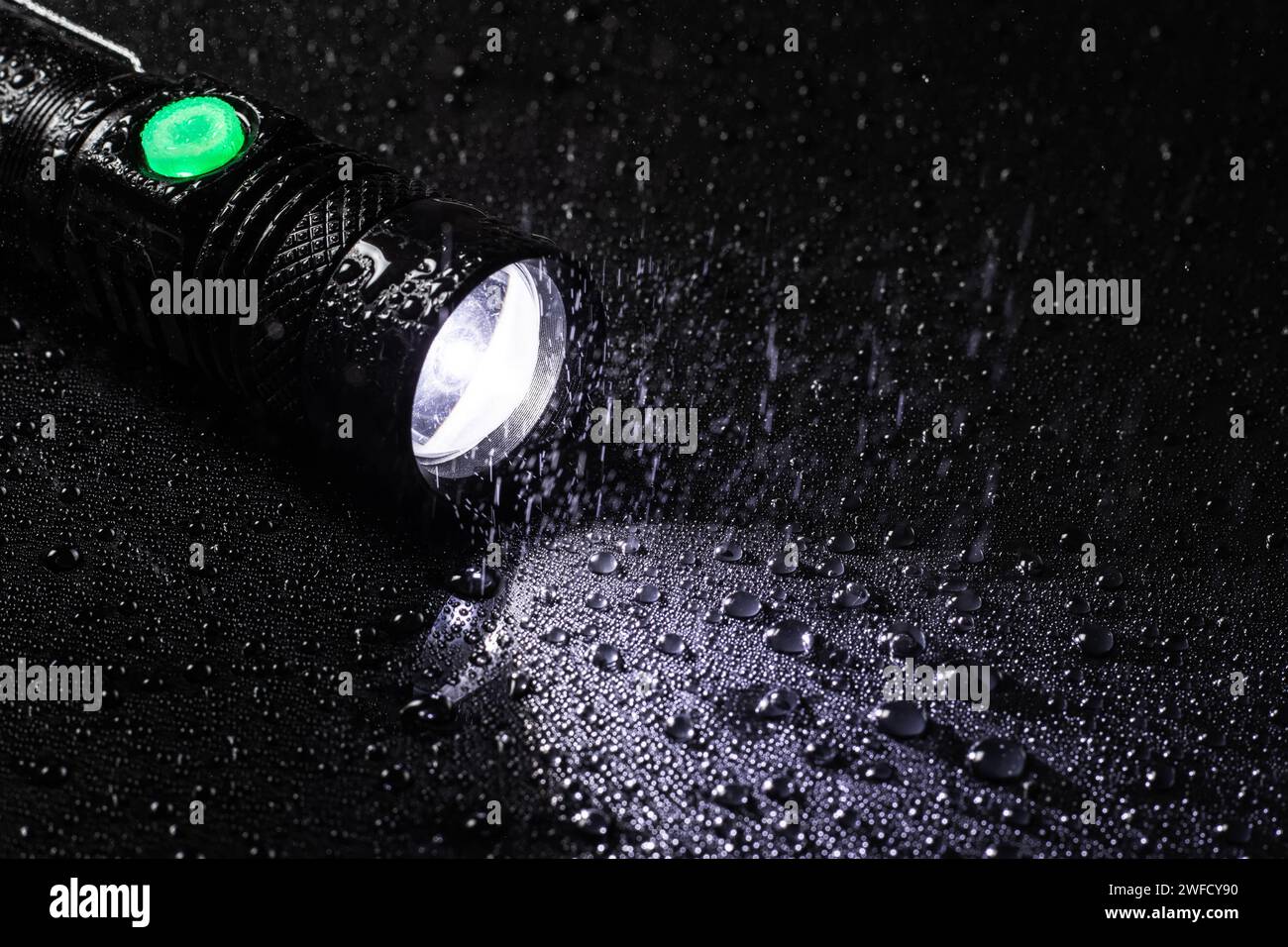 LED Flashlight water resistant in drops and rain on black background ...