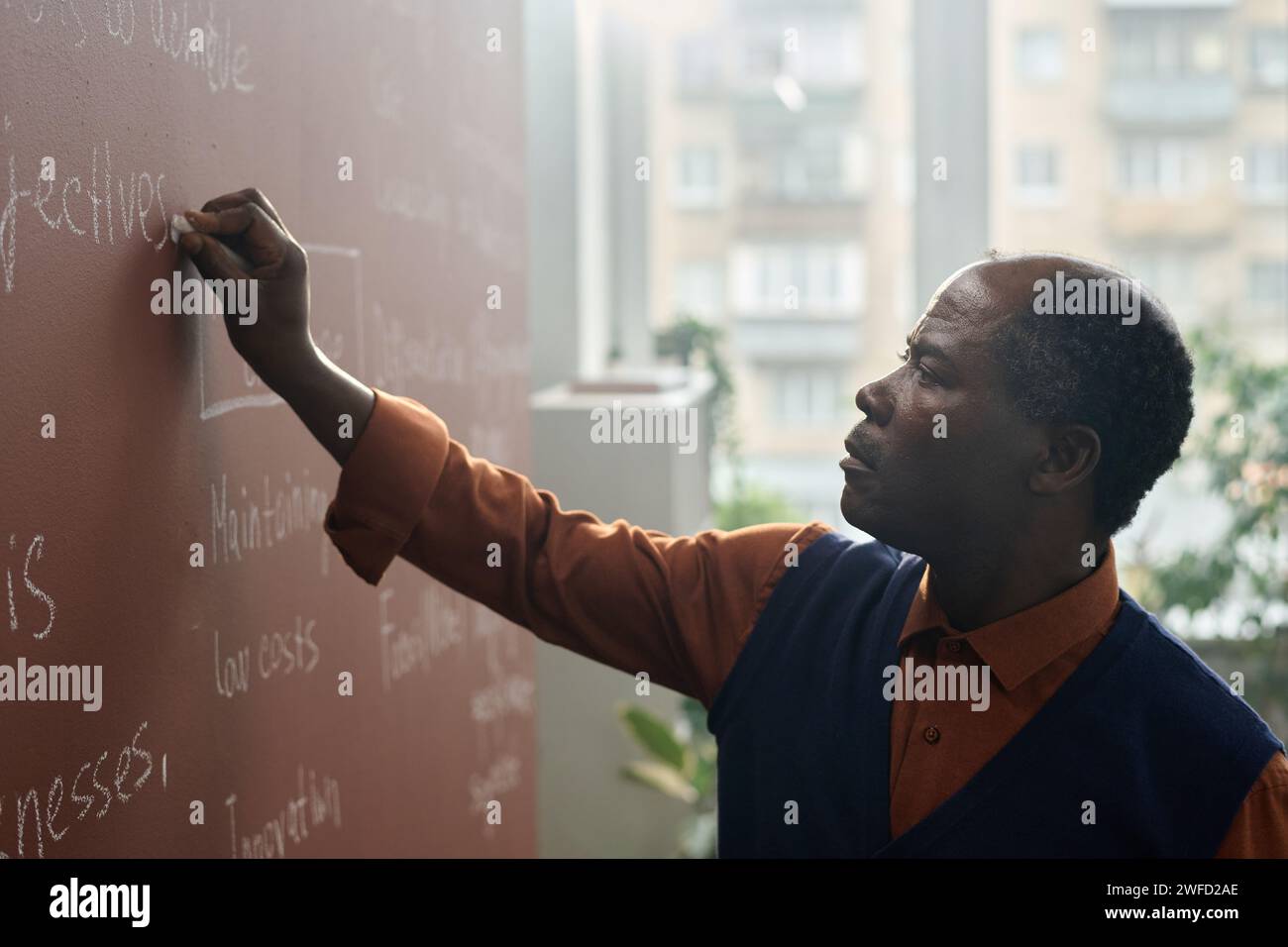 Side view portrait of Black college professor writing on chalkboard ...