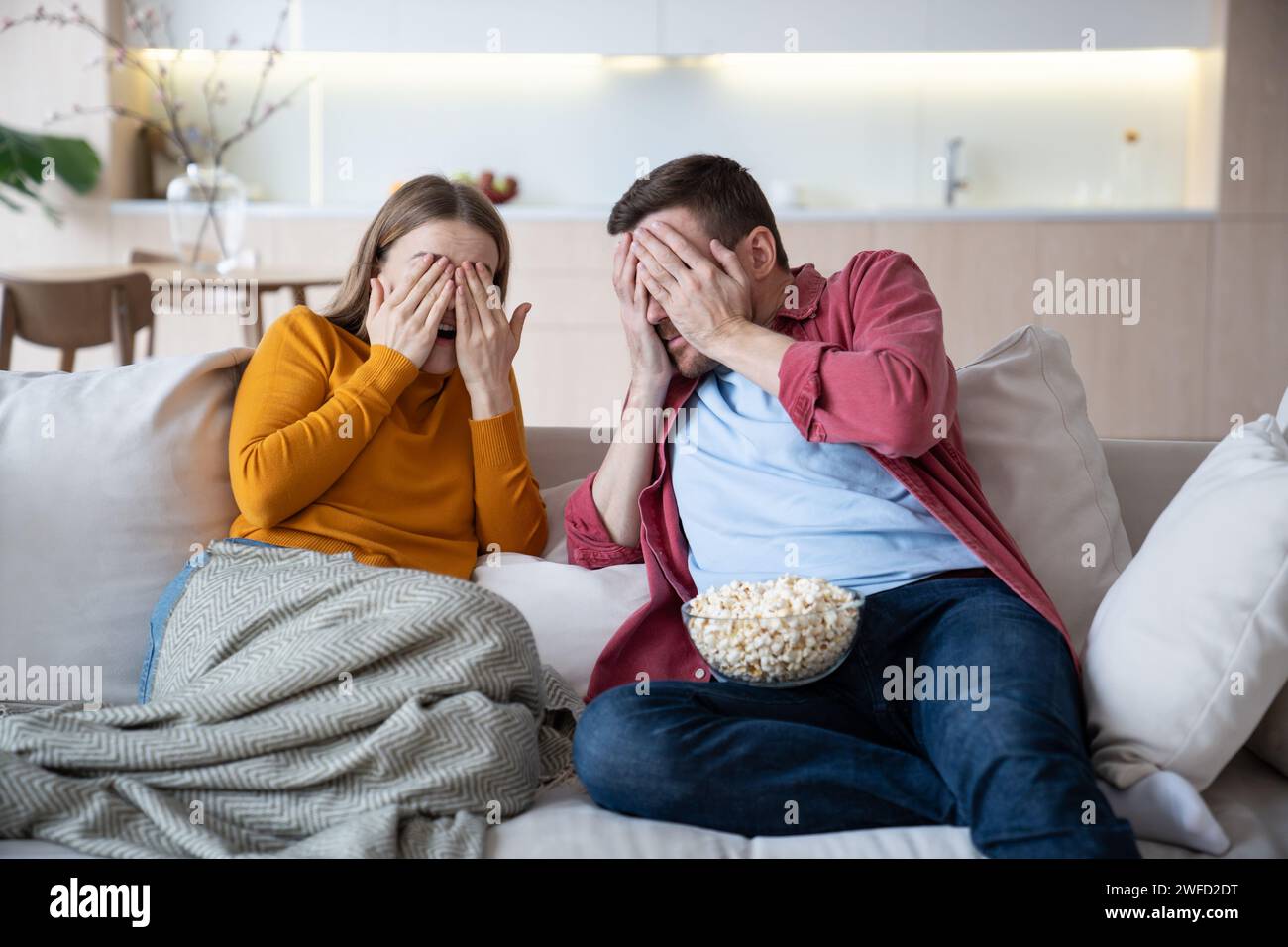 Scared family couple cover eyes with palms watching horrifying movie ...