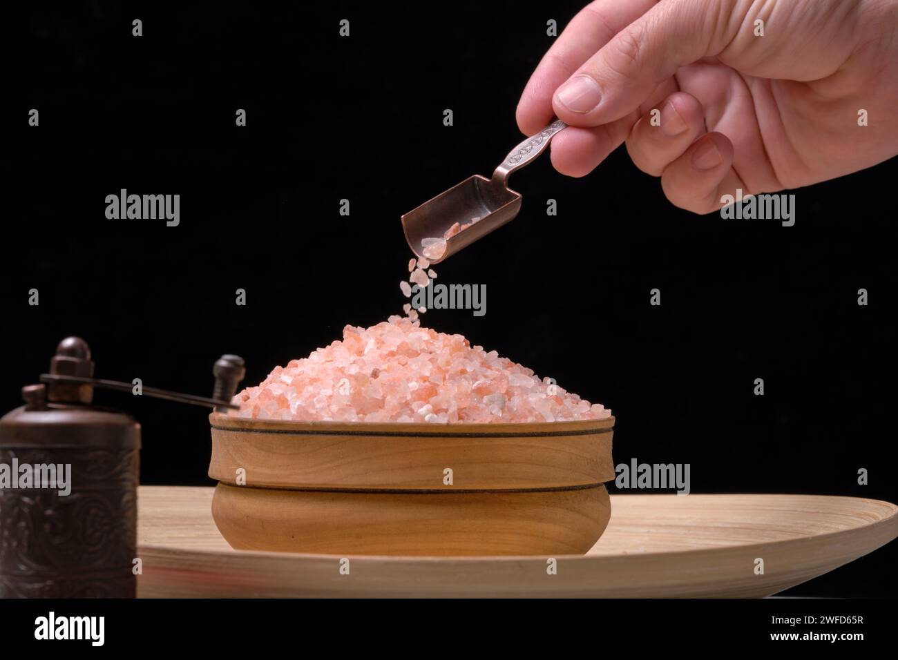 In his hand, spice spoon is pouring pink salt into cup on black ...