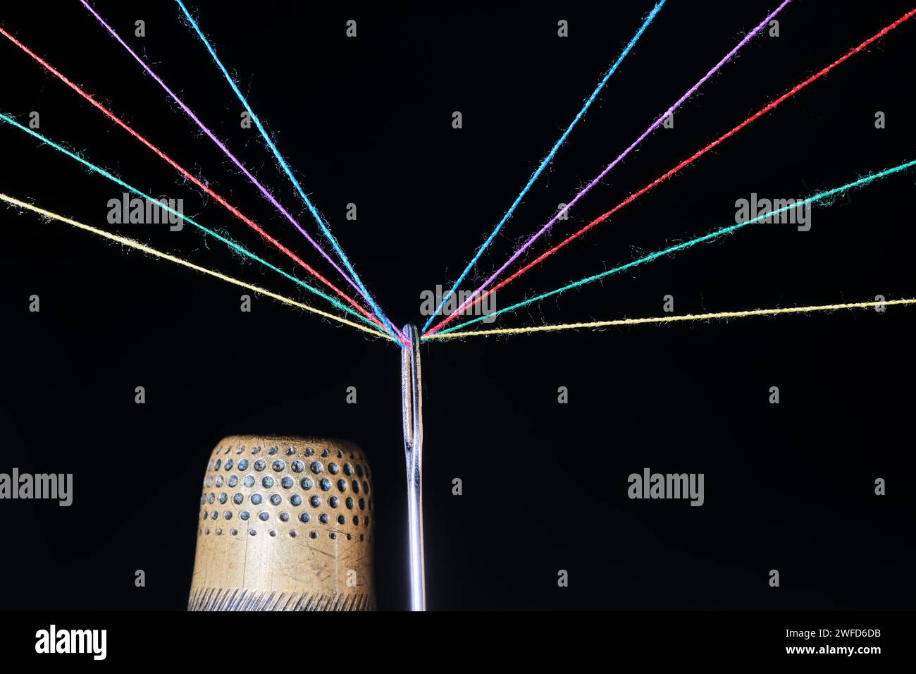 Thimble, eye sewing needle and multicolored threads passed through it ...