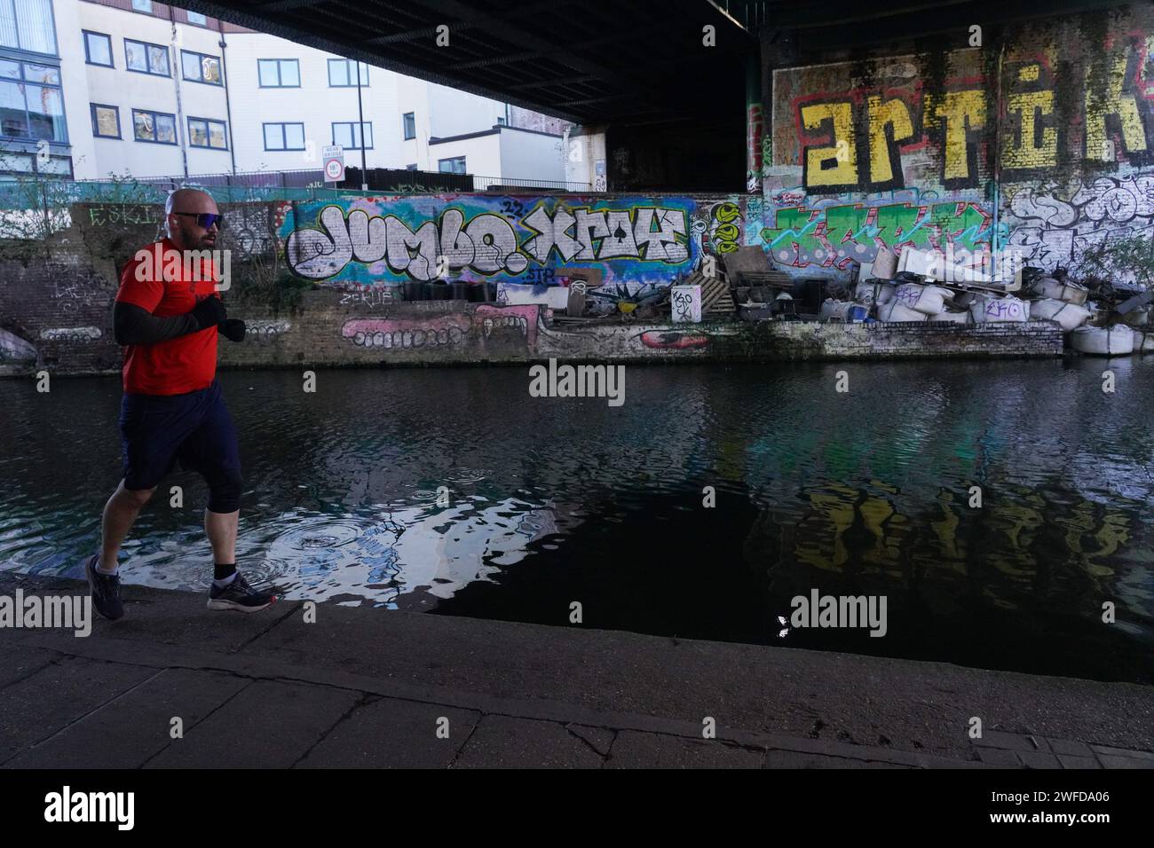A man runs along the tow path by the Regent's Canal under a bridge in ...