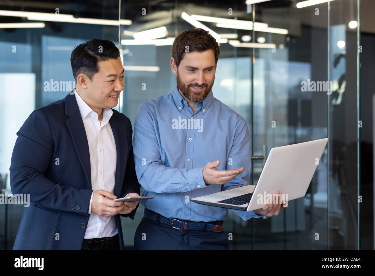 Two professional businessmen collaborate using a laptop in a contemporary office environment ...