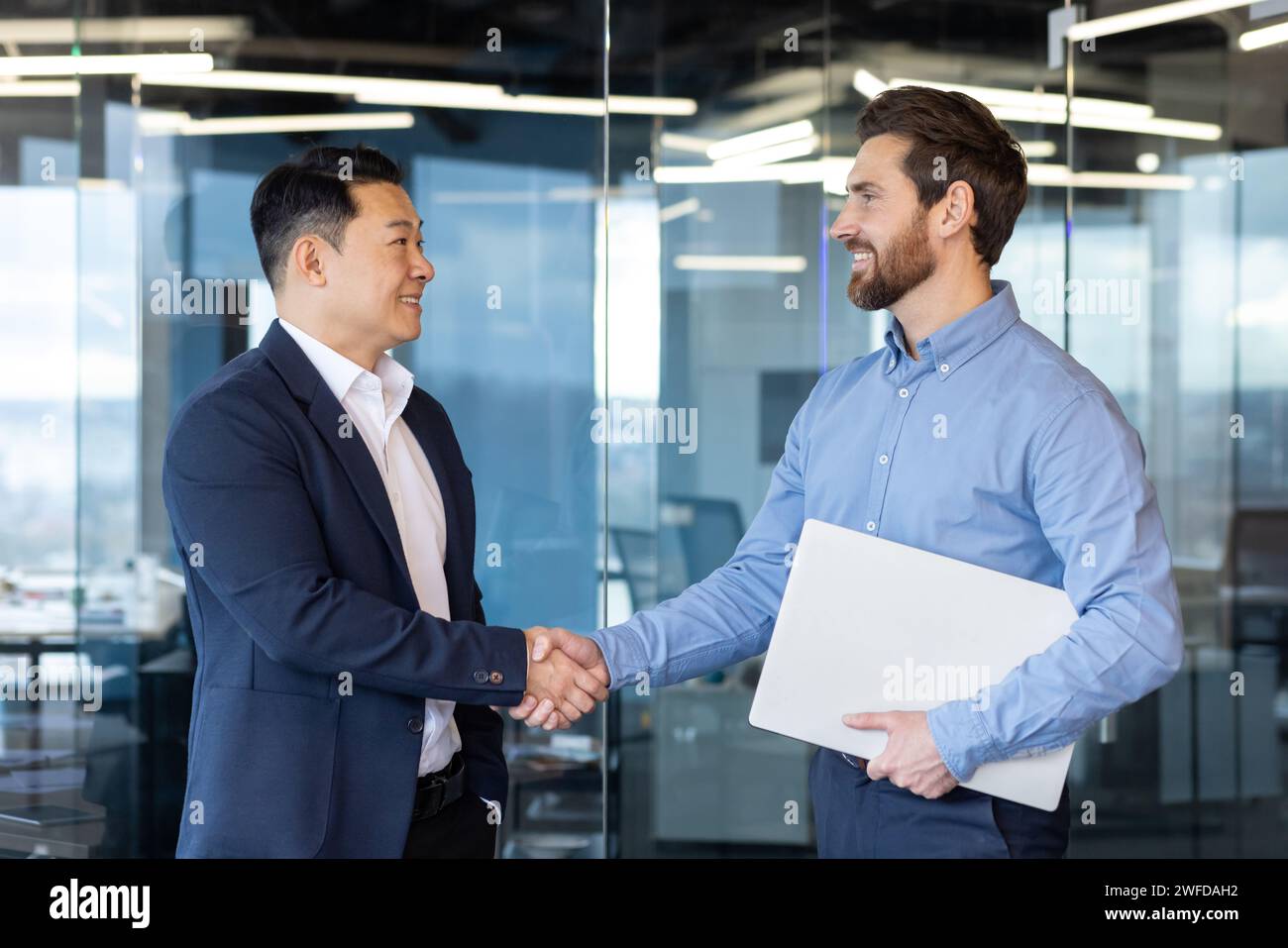 Professional and friendly handshake between two businessmen in an office setting, symbolizing ...