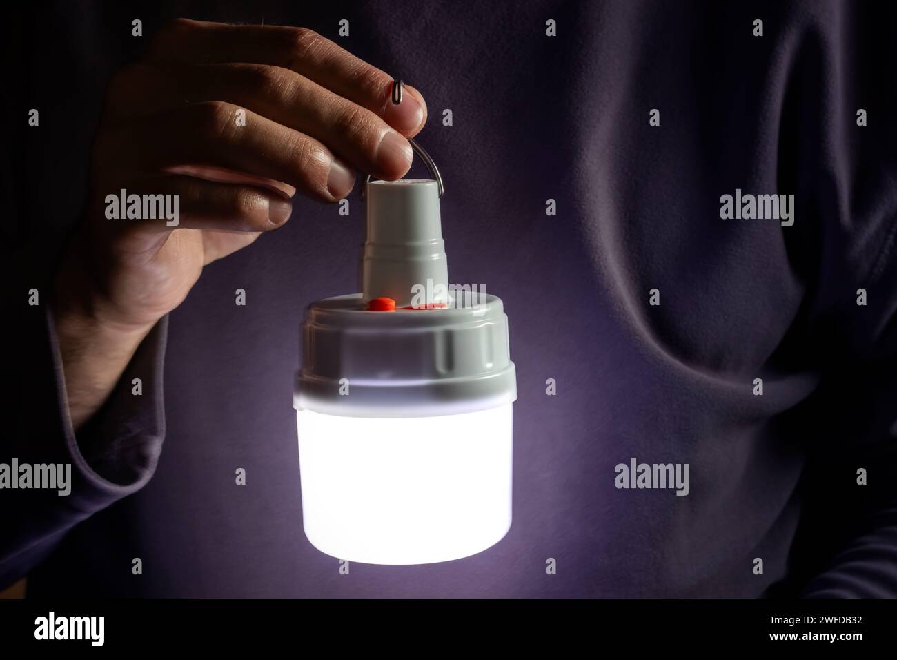 A man's hand holds a portable rechargeable LED emergency light with a ...