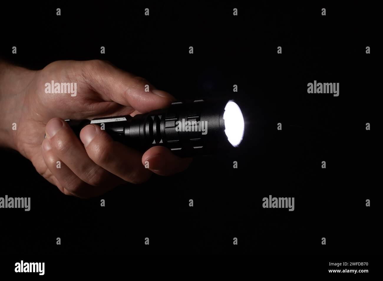 Male hand holding a led flashlight with a wide white beam on a black ...