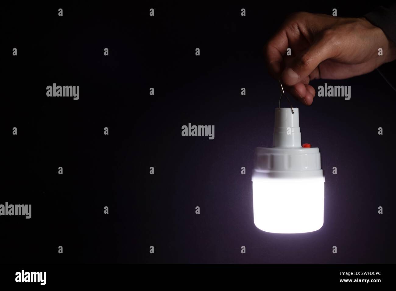 A man's hand holds a portable rechargeable LED emergency light with a ...