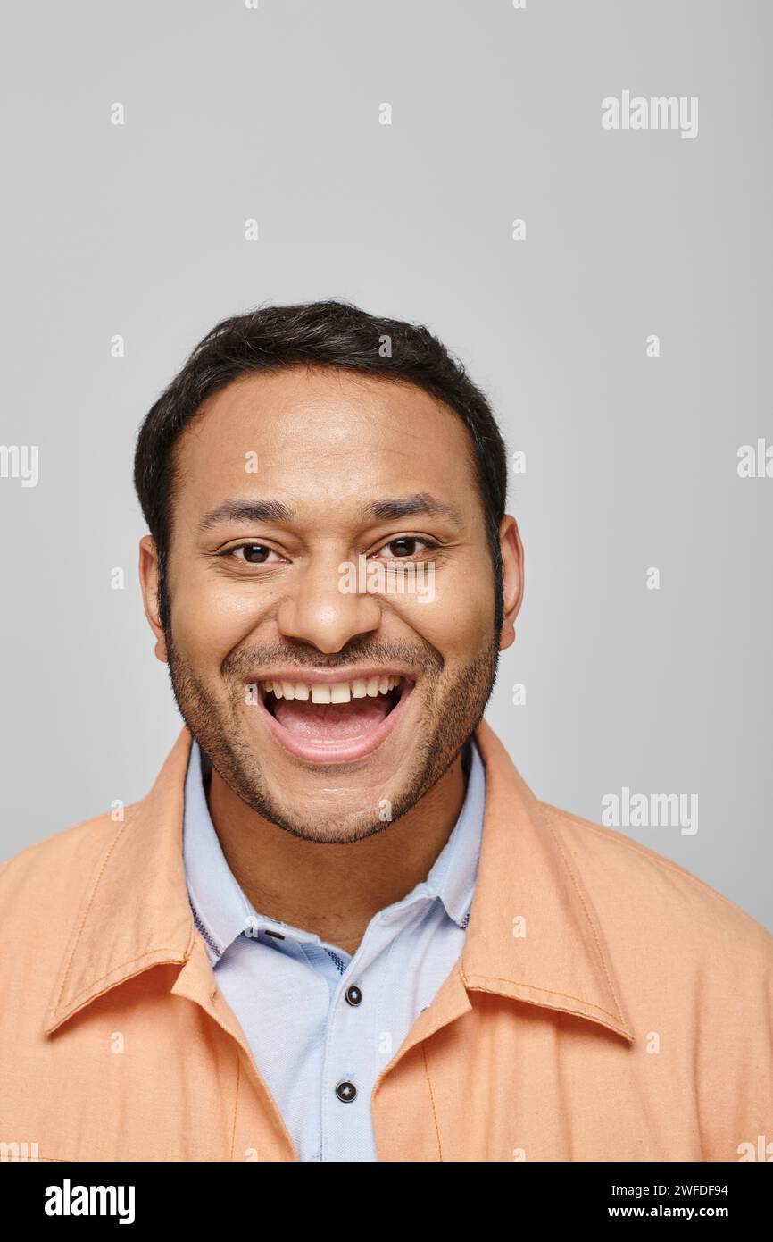 cheerful handsome indian man in orange jacket smiling straight at ...