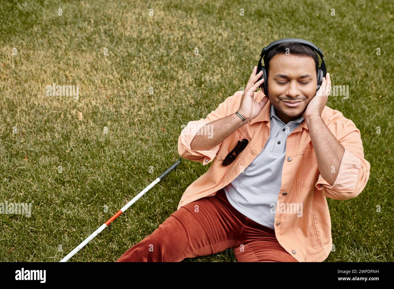 cheerful indian disabled man in orange jacket sitting on grass with ...