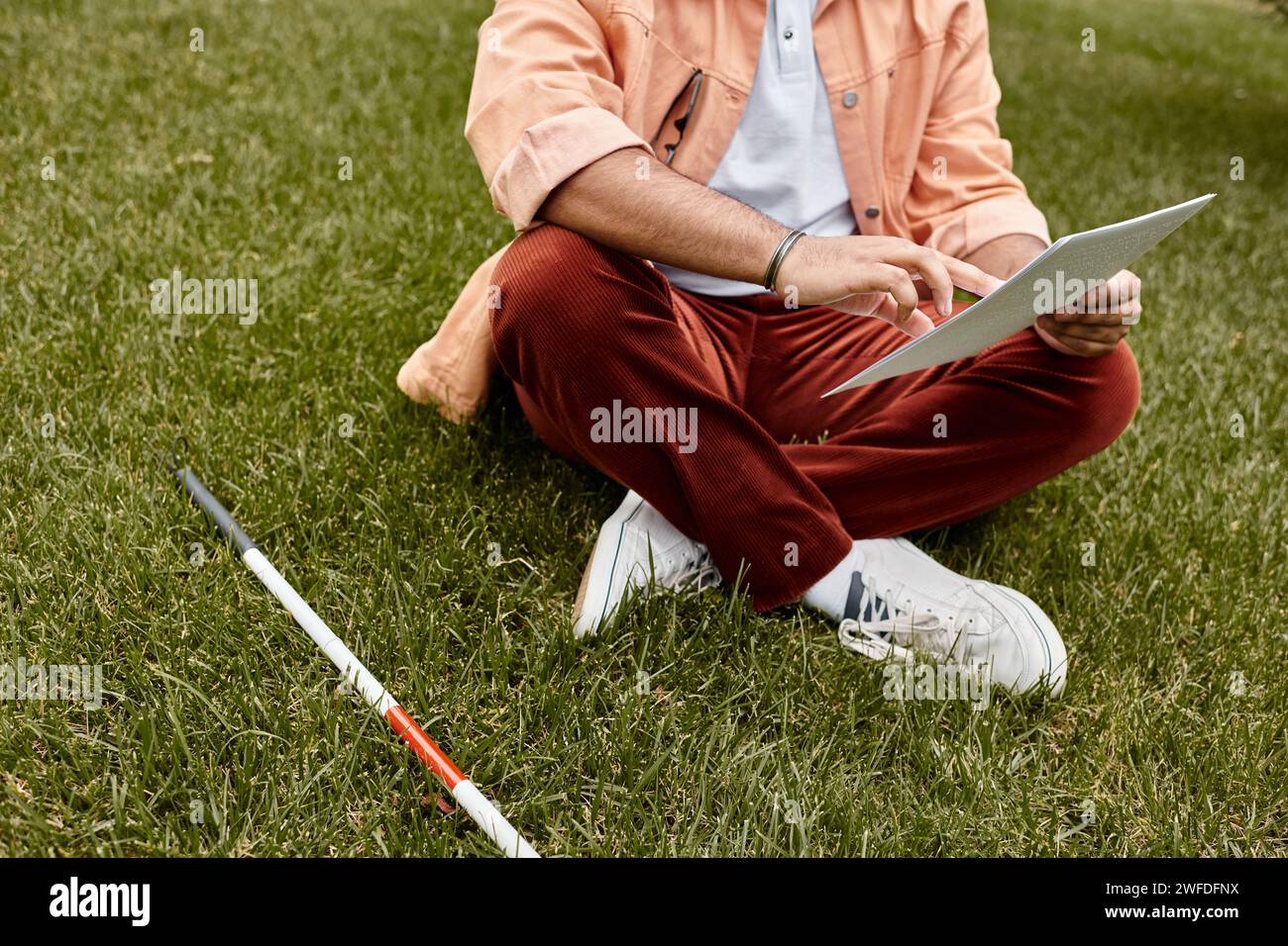 cropped view of blind indian man in orange jacket sitting on grass and ...