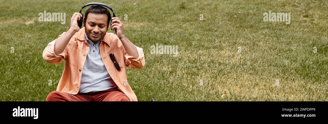 cheerful indian blind man in orange jacket sitting on grass with ...