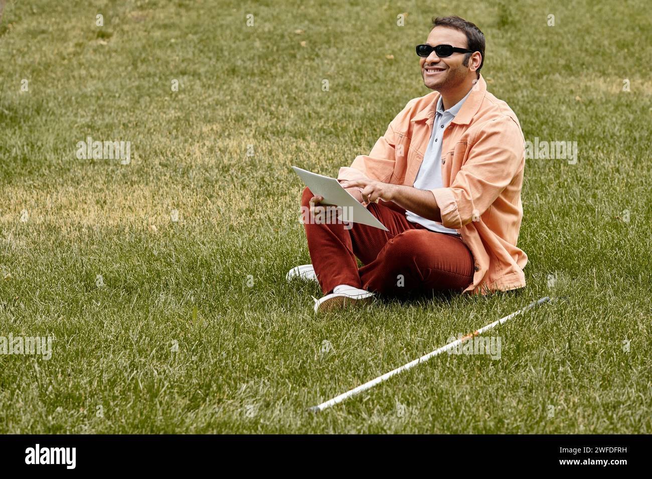 merry indian blind man in orange vivid jacket sitting on grass with ...