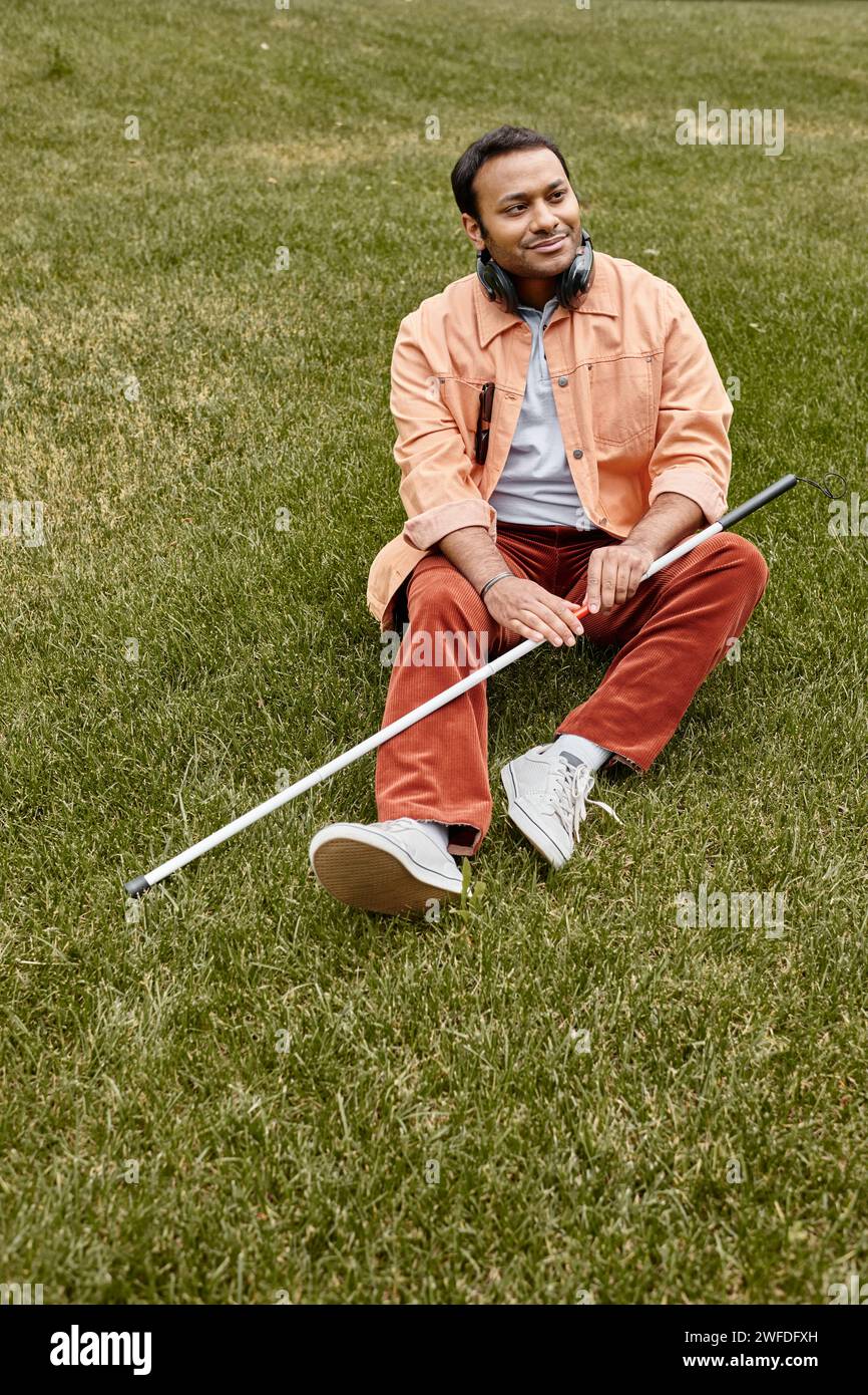 joyful indian blind man in orange jacket sitting on grass with ...