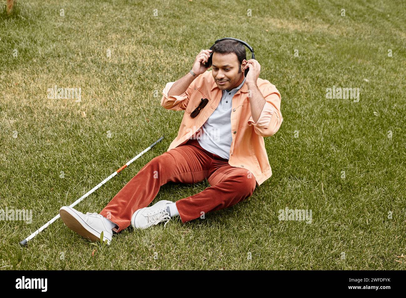 joyous indian blind man in orange jacket sitting on grass with ...