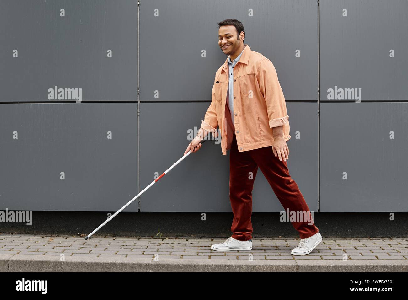 cheerful indian blind man in orange jacket with helping stick walking ...