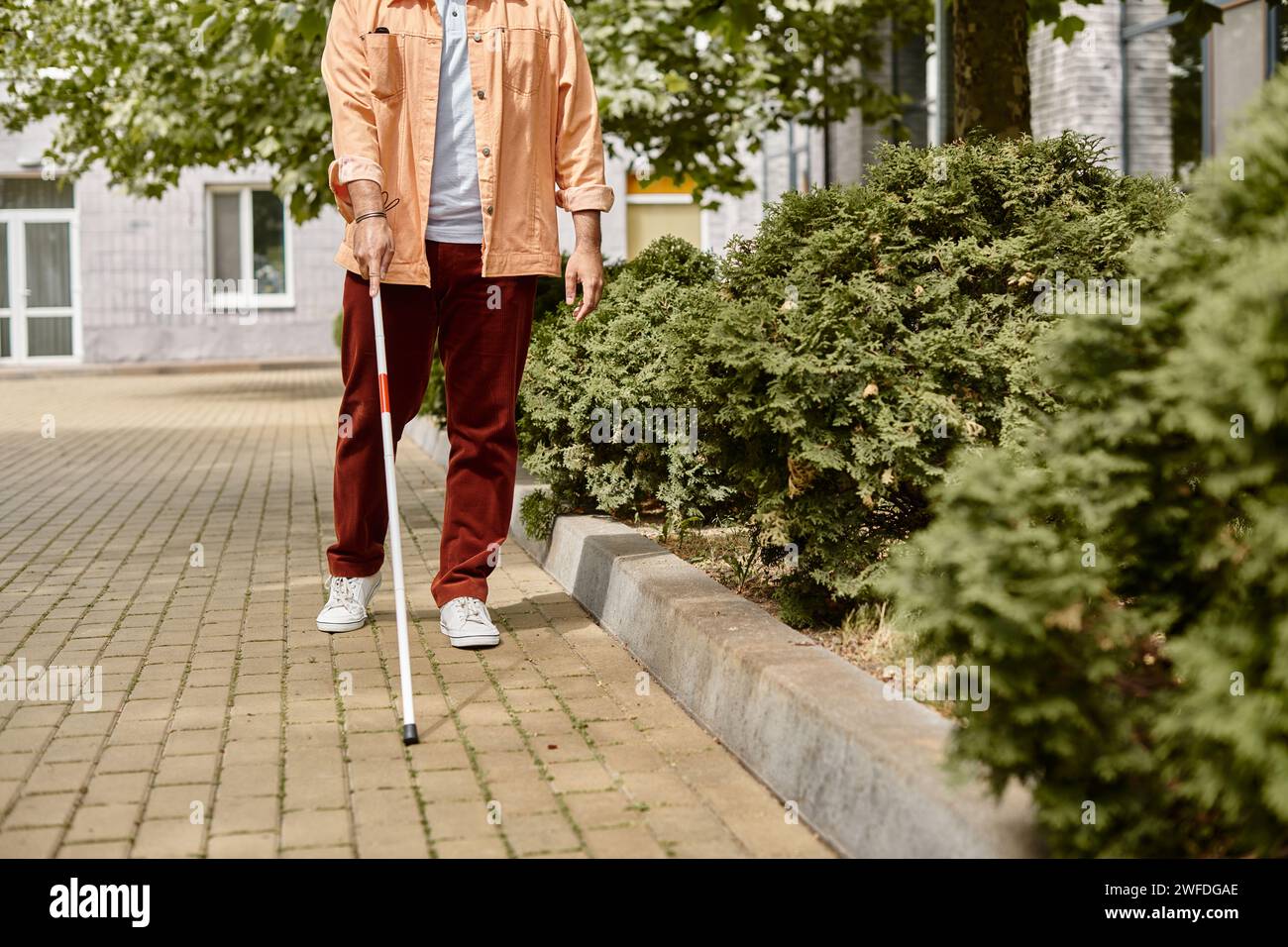 cropped view of indian disabled man in orange jacket with walking stick ...