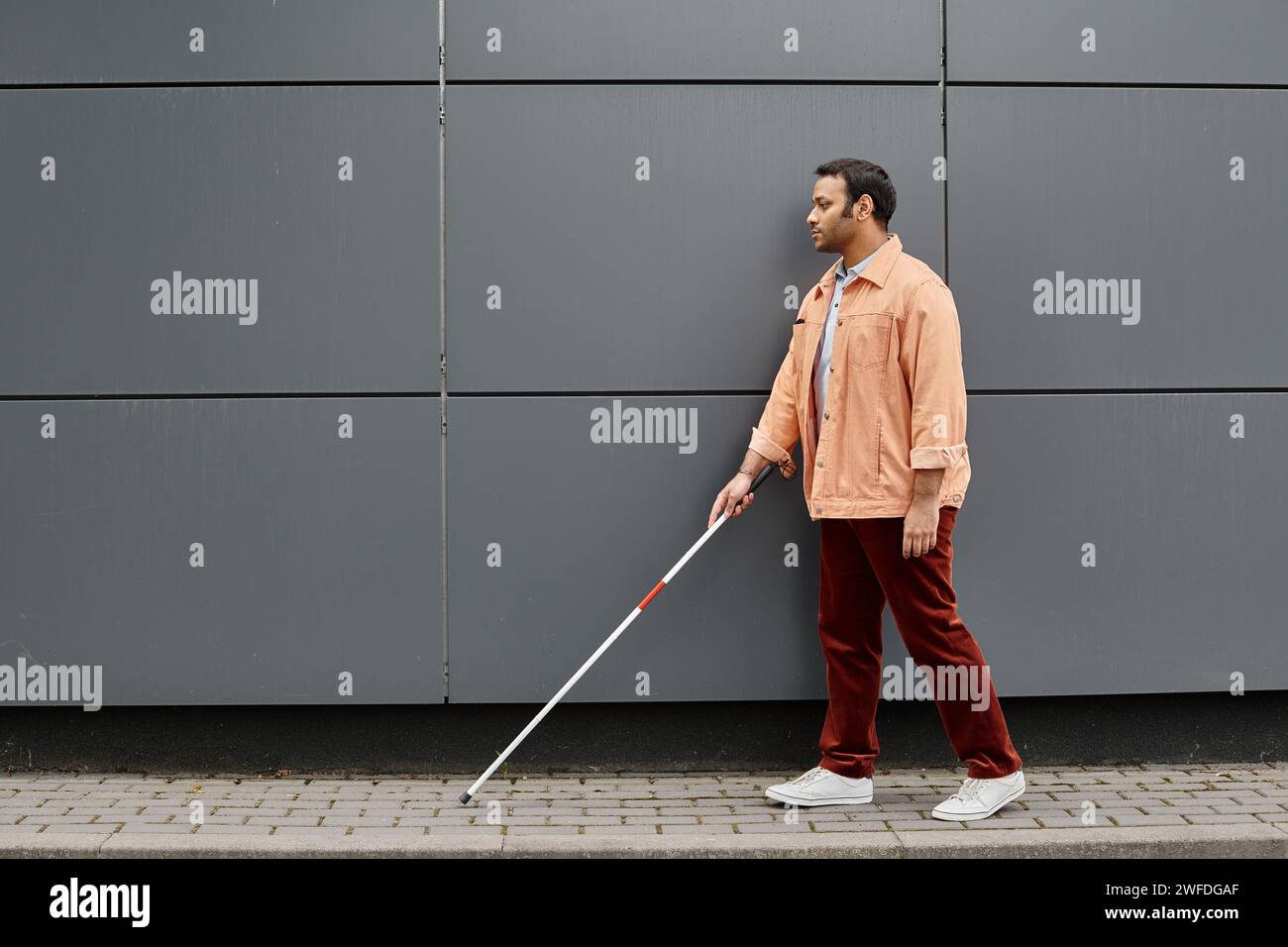 attractive indian blind man in orange jacket with helping stick walking ...