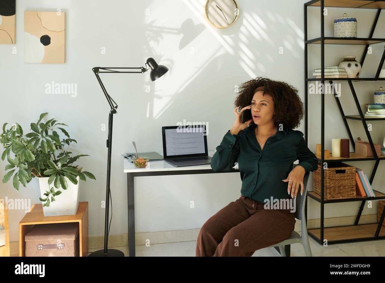 Software developer sitting at her home office desk and talking on phone ...