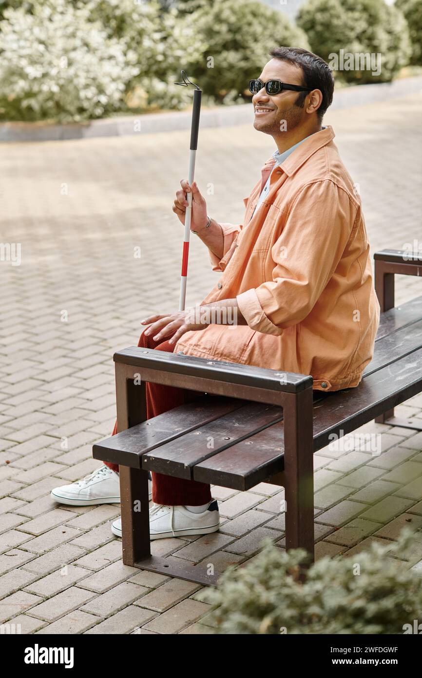 joyous indian blind man in orange jacket sitting outside on bench with ...