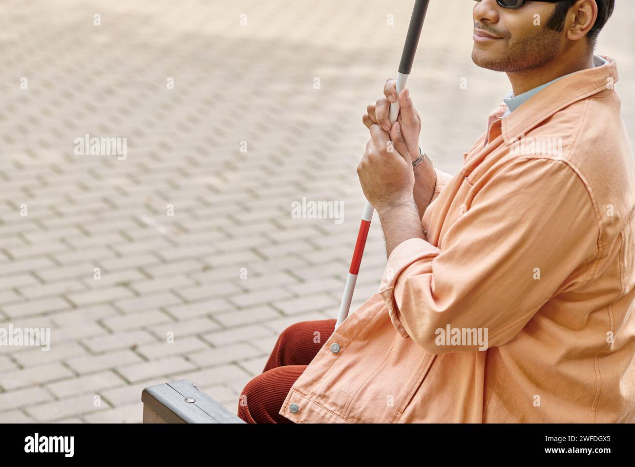 cheerful indian blind man in orange jacket sitting outside on bench ...