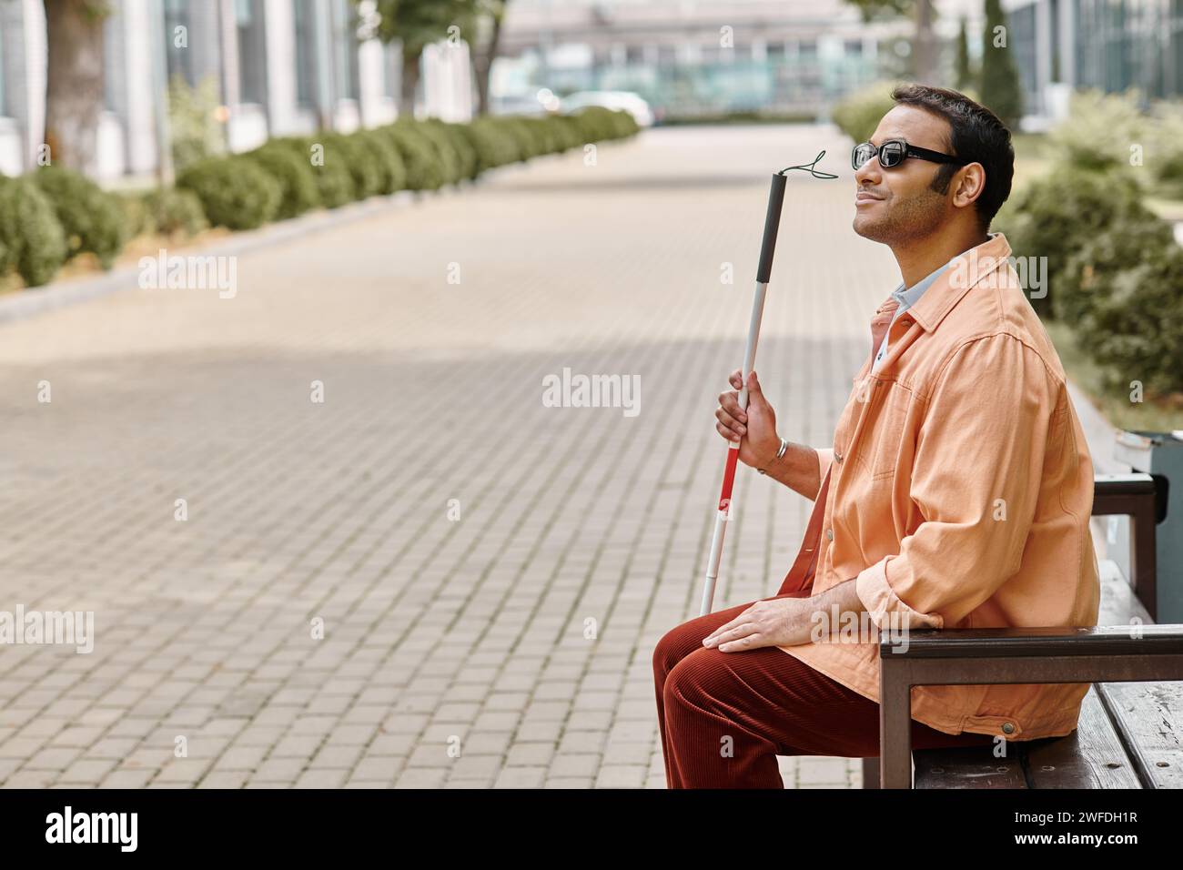 glad indian blind man in orange jacket sitting outside on bench with ...