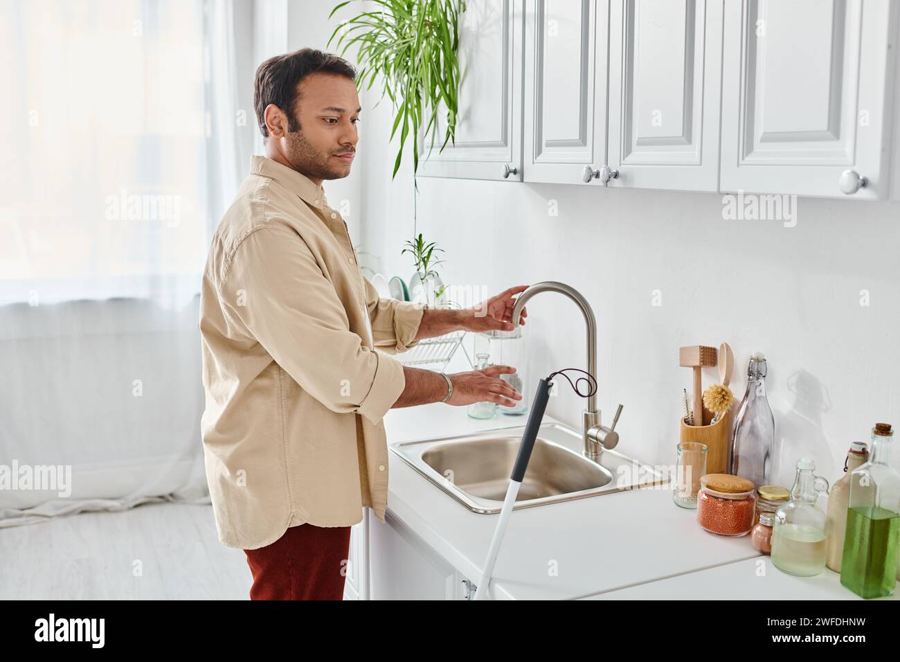 good looking indian man with visual impairment pouring some tap water ...