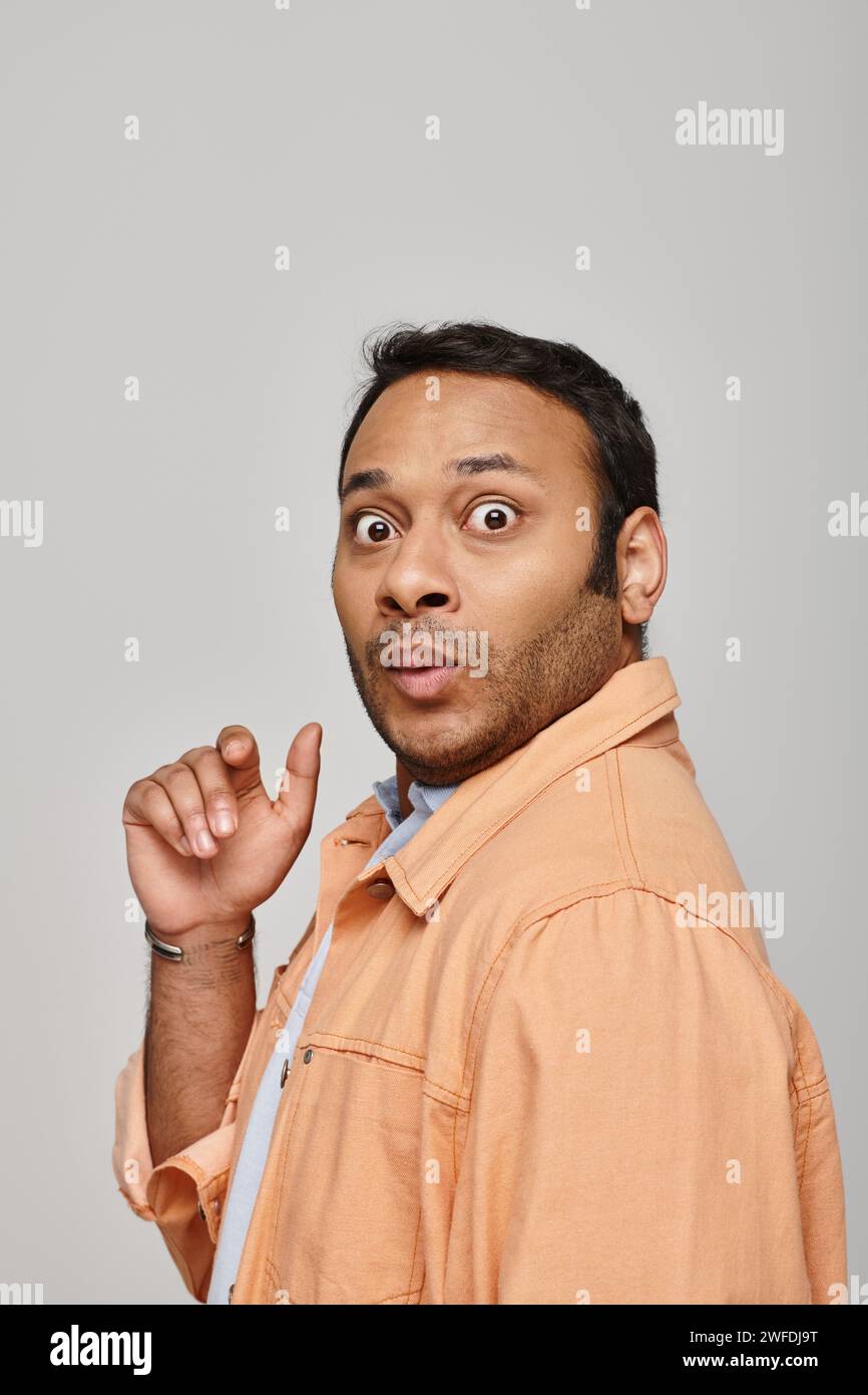 shocked handsome indian man in orange jacket posing with raised hand ...